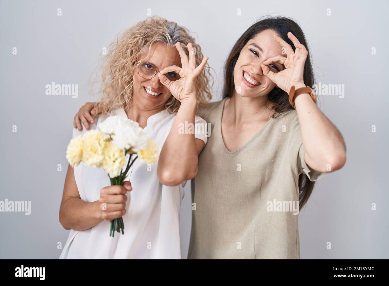 Mother and daughter holding bouquet of white flowers doing ok gesture ...