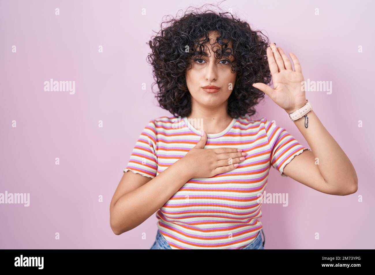Young middle east woman standing over pink background swearing with ...