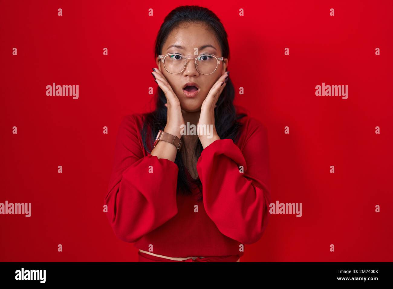 Asian young woman standing over red background afraid and shocked ...