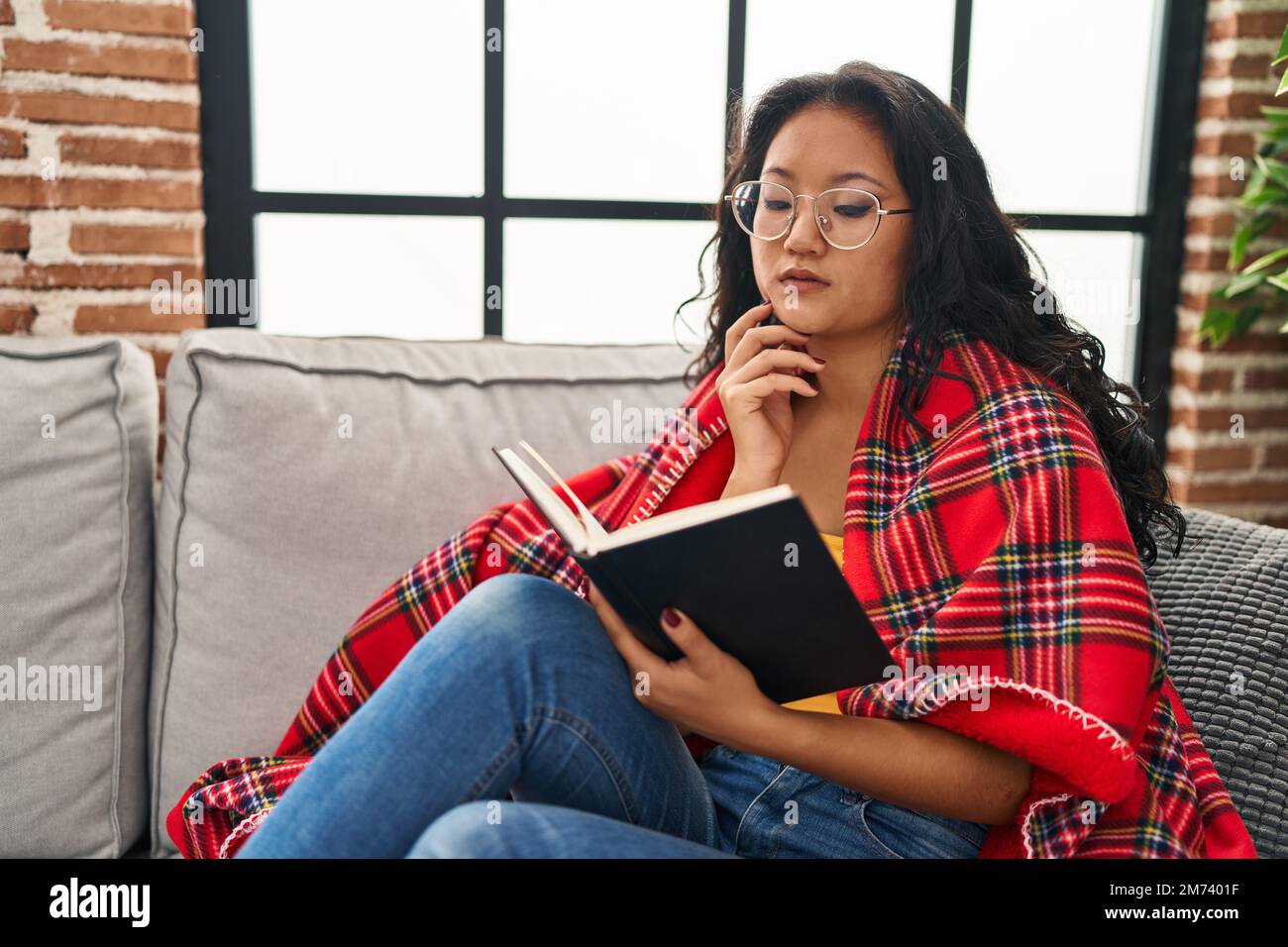Young chinese woman reading book sitting on sofa at home Stock Photo ...