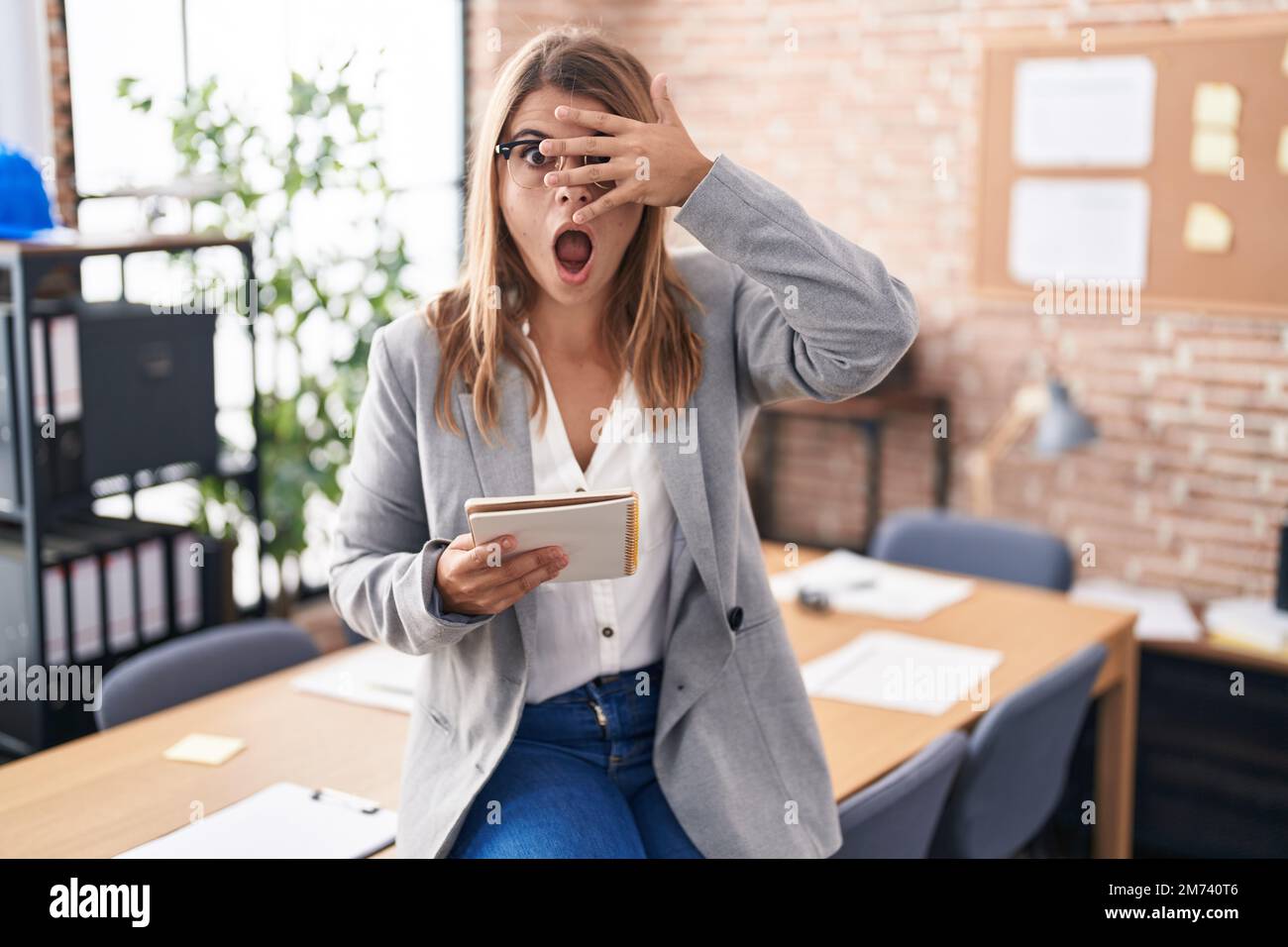 Young hispanic woman working at the office wearing glasses peeking in ...