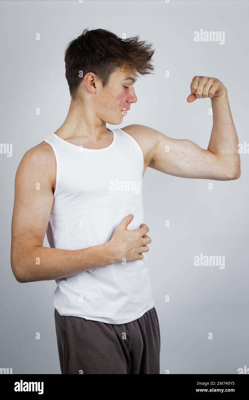 A 17 year old teenage boy wearing a white tank top flexing his arm ...
