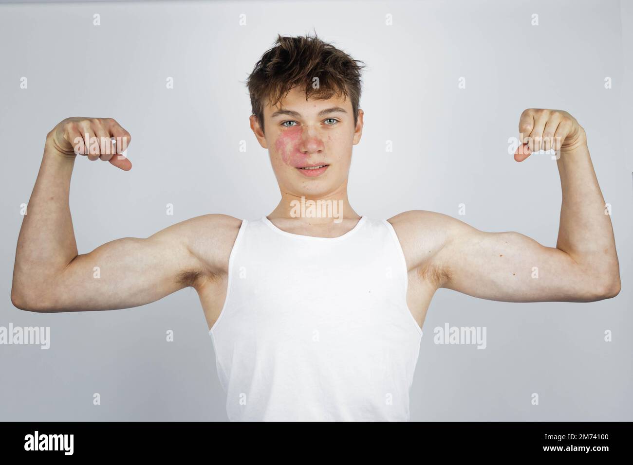 A 17 year old teenage boy wearing a white tank top flexing his arm ...