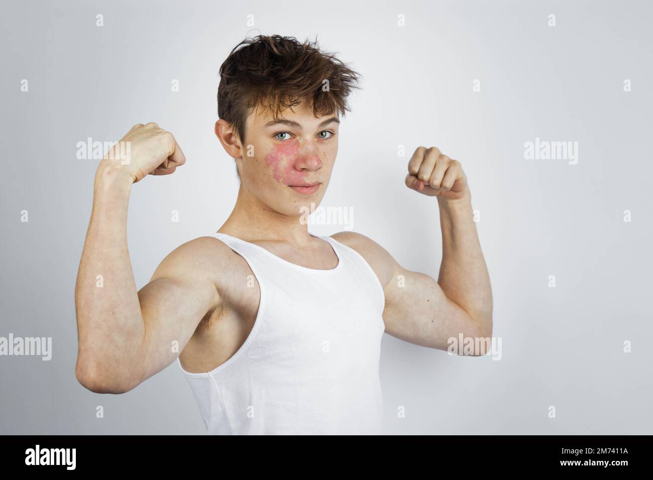 A 17 year old teenage boy wearing a white tank top flexing his arm ...