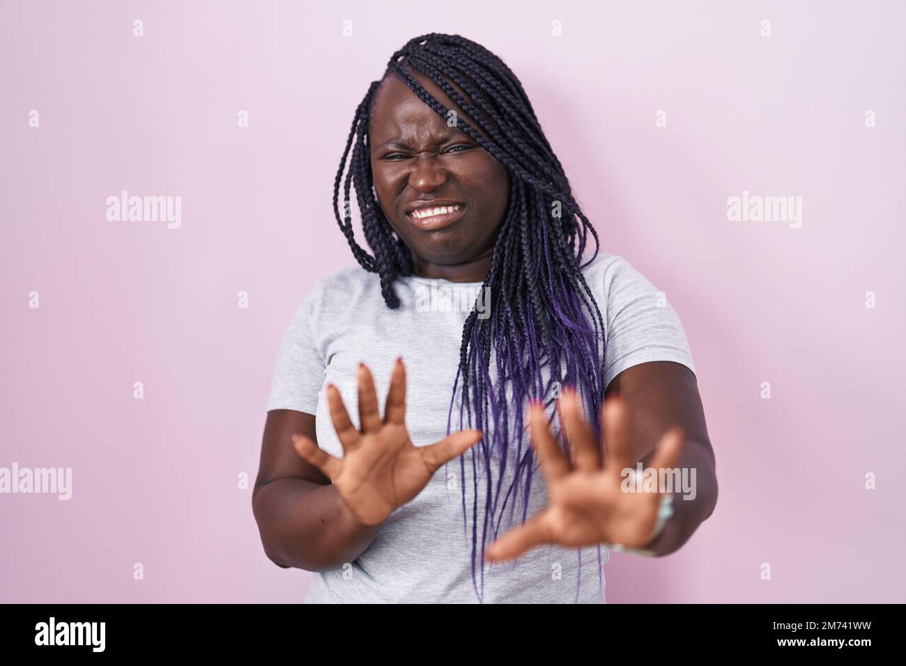 Young african woman standing over pink background disgusted expression ...
