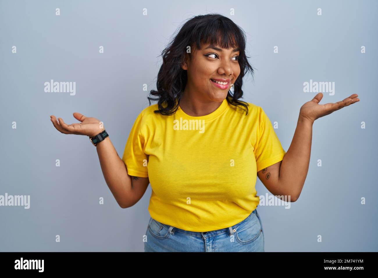 Hispanic woman standing over blue background smiling showing both hands ...