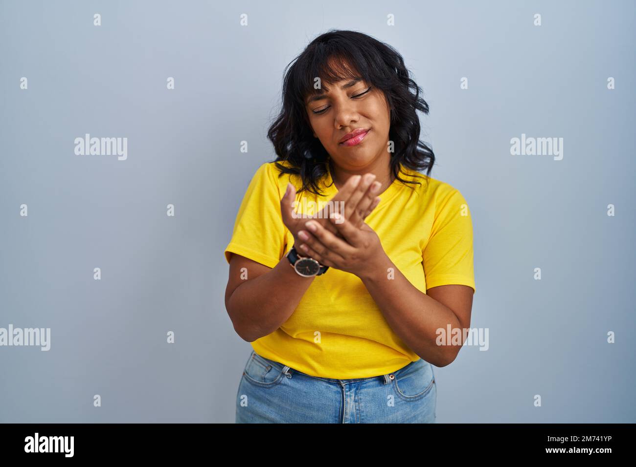 Hispanic woman standing over blue background suffering pain on hands ...