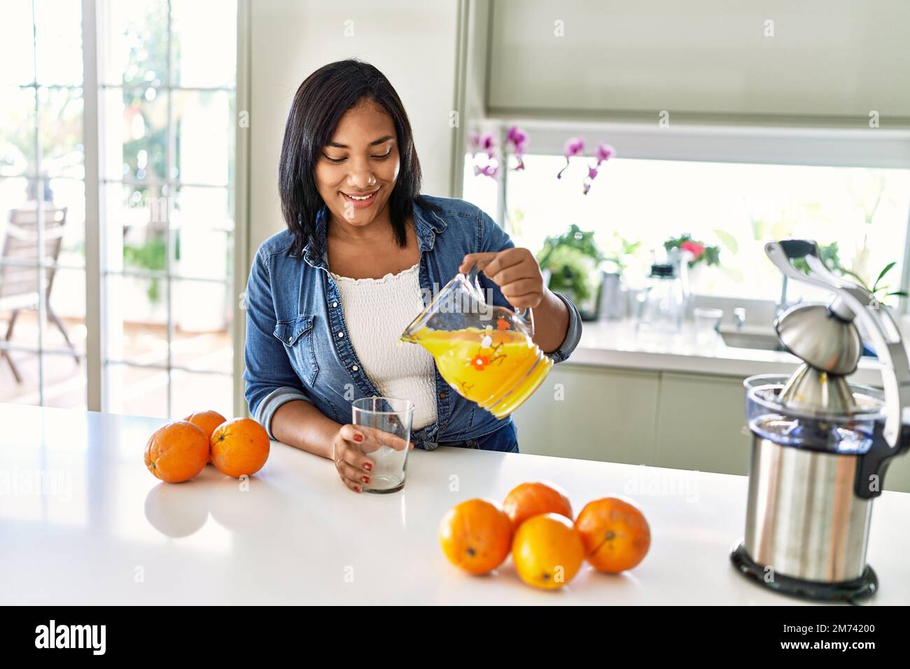 Hispanic brunette woman drinking a glass of fresh orange juice at the ...