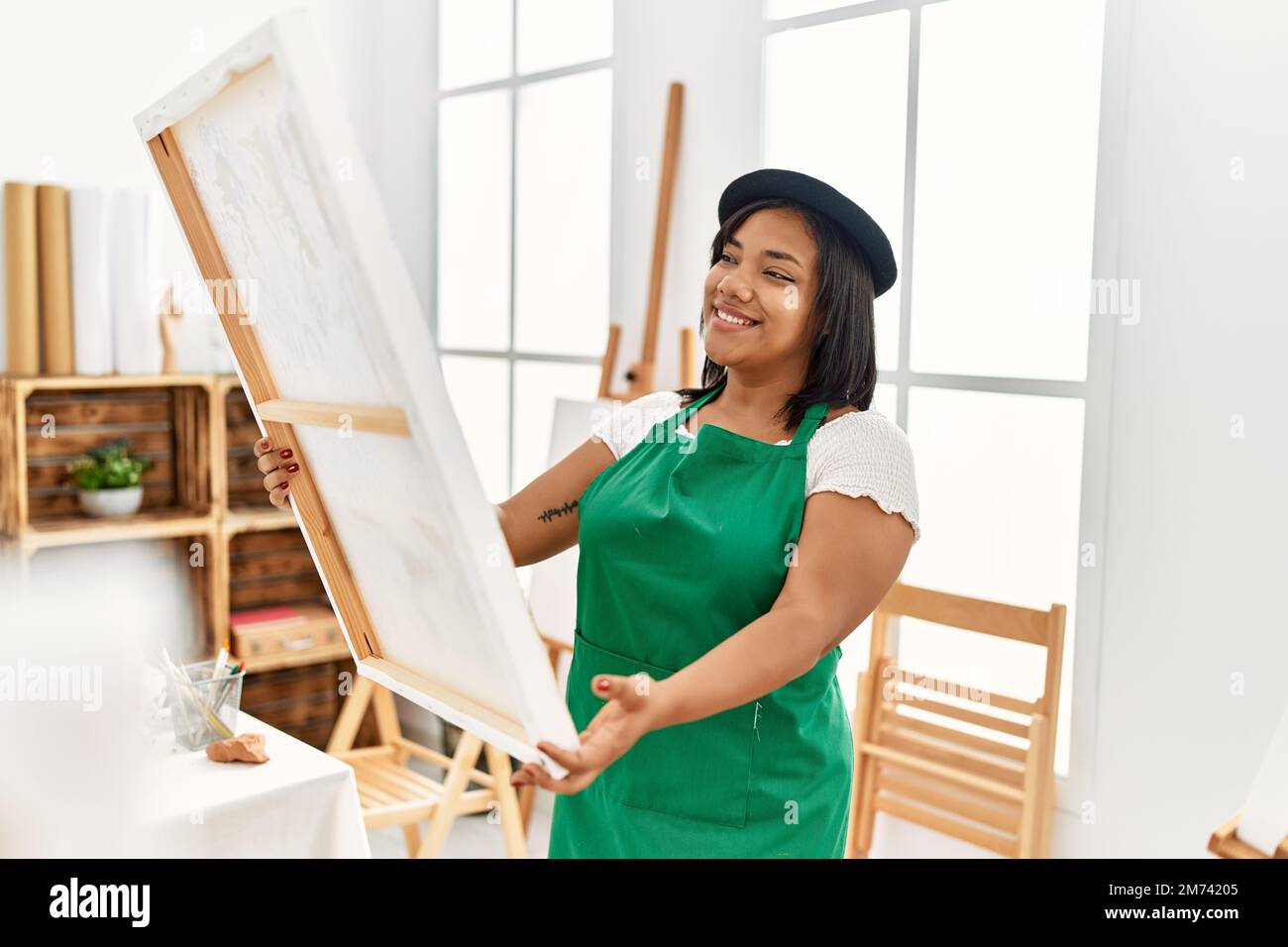 Hispanic brunette woman holding canvas proud of painting at art studio ...