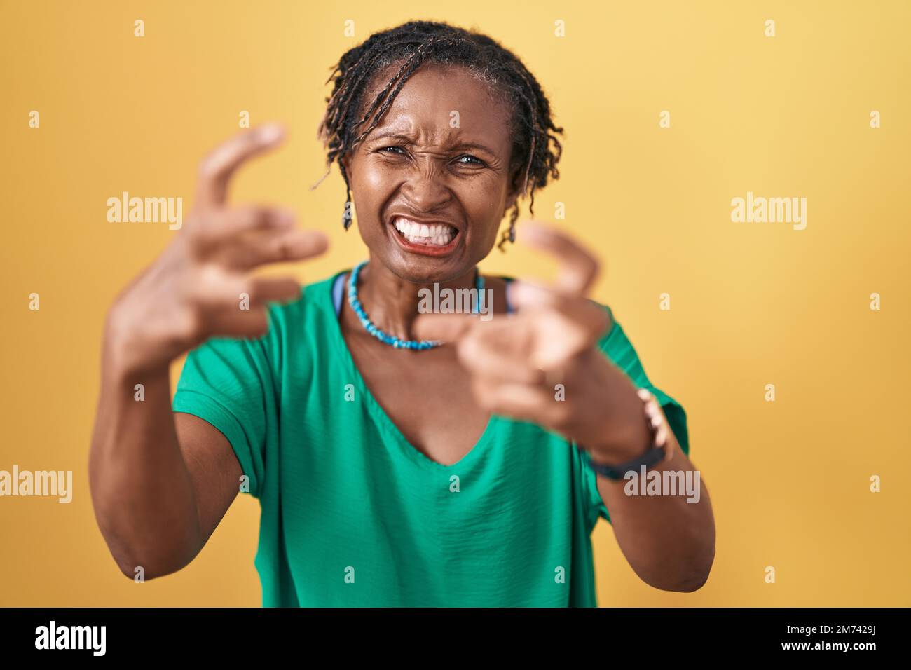 African woman with dreadlocks standing over yellow background shouting ...
