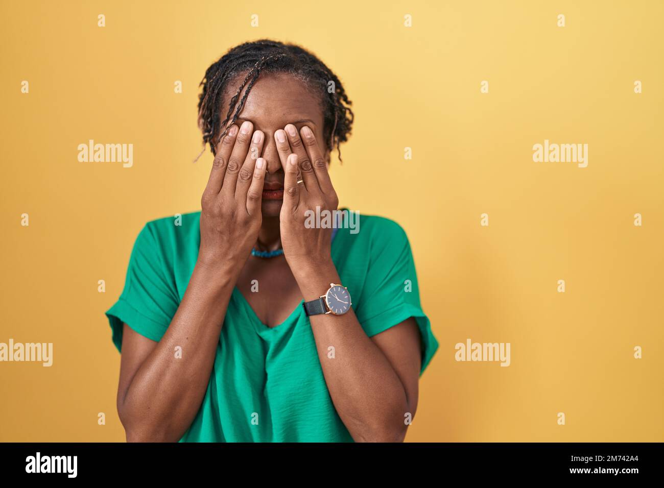African woman with dreadlocks standing over yellow background rubbing ...