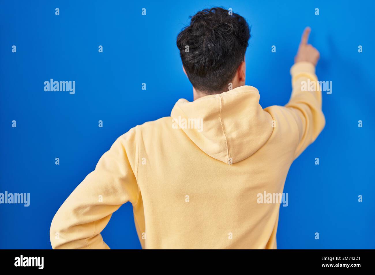 Hispanic man standing over blue background posing backwards pointing ...