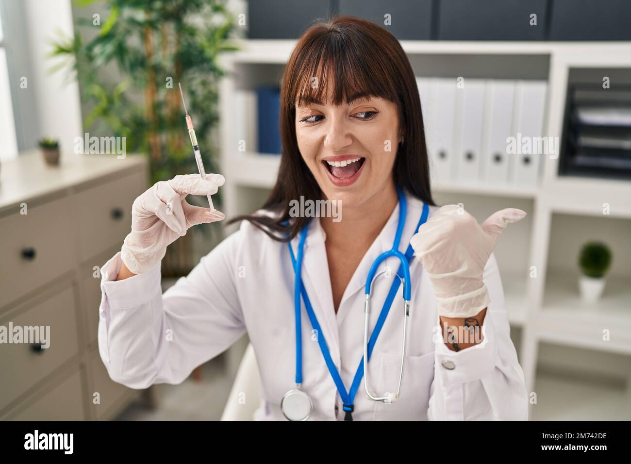 Young brunette doctor woman holding syringe pointing thumb up to the ...