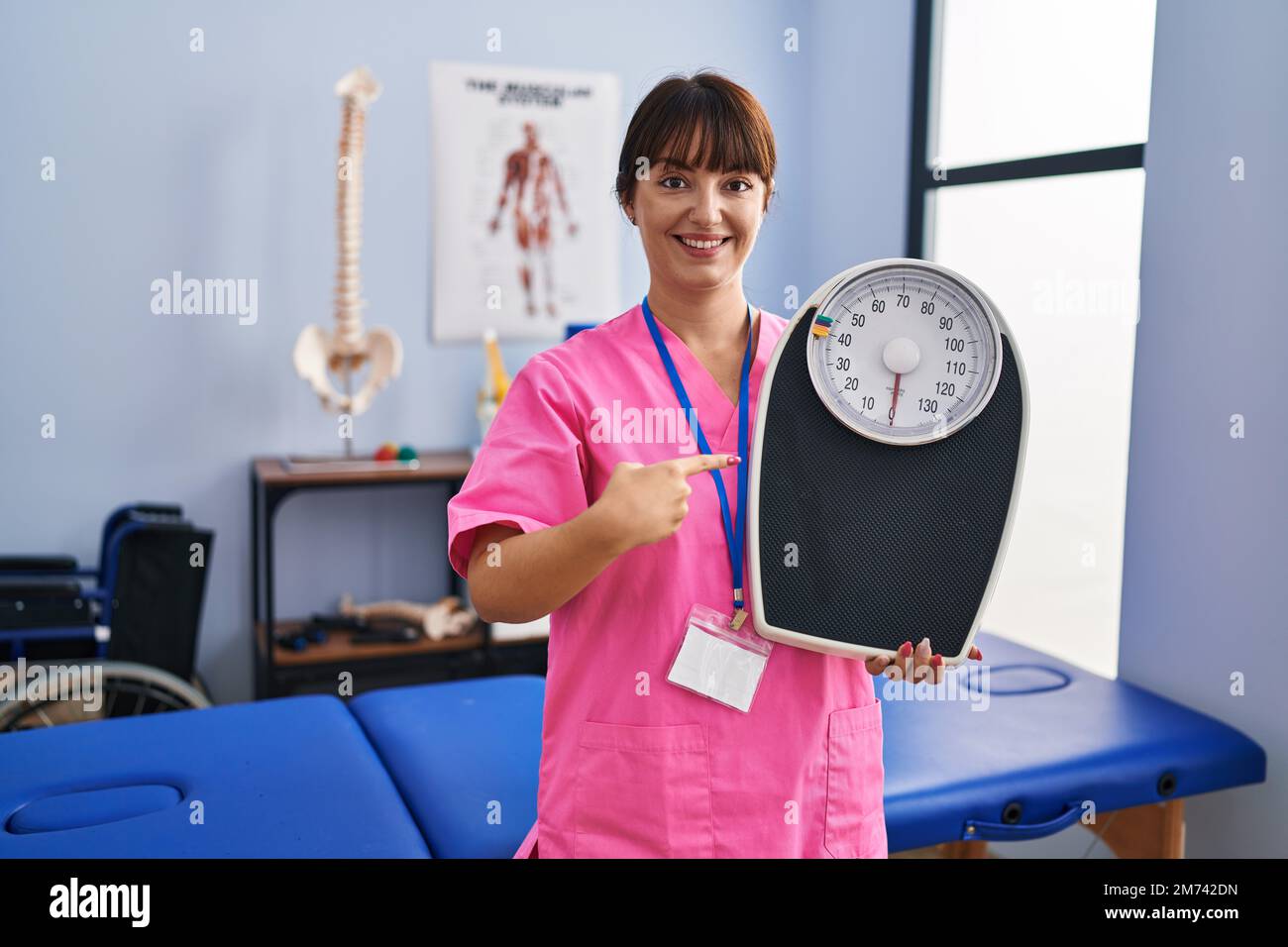 Young brunette woman as nutritionist holding weighing machine smiling ...