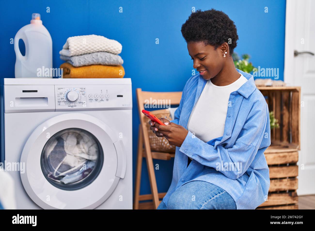 African american woman using smartphone waiting for washing machine at ...