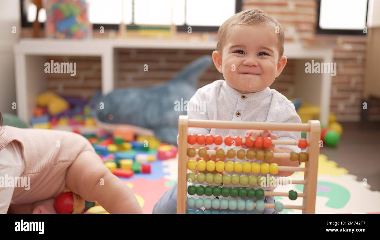 Adorable toddler playing with abacus sitting on floor at kindergarten ...