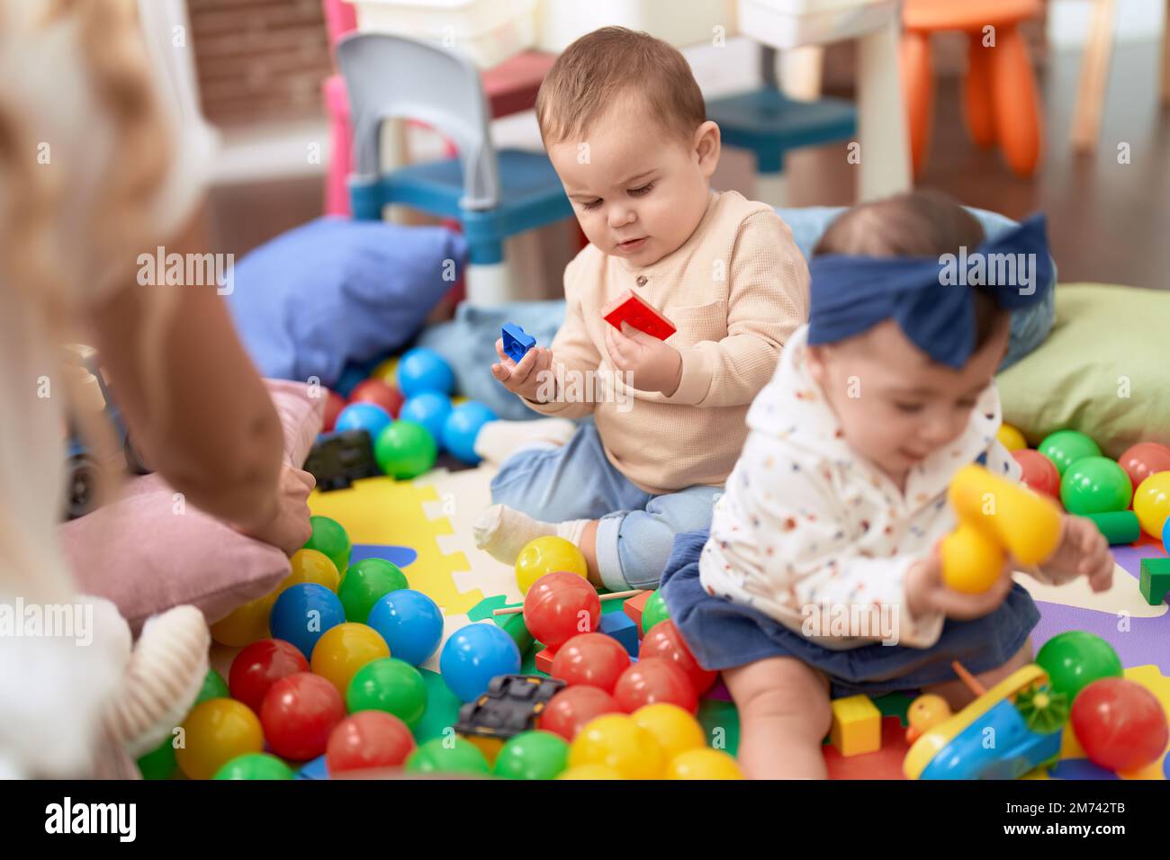 Two toddlers playing with toys sitting on floor at kindergarten Stock ...