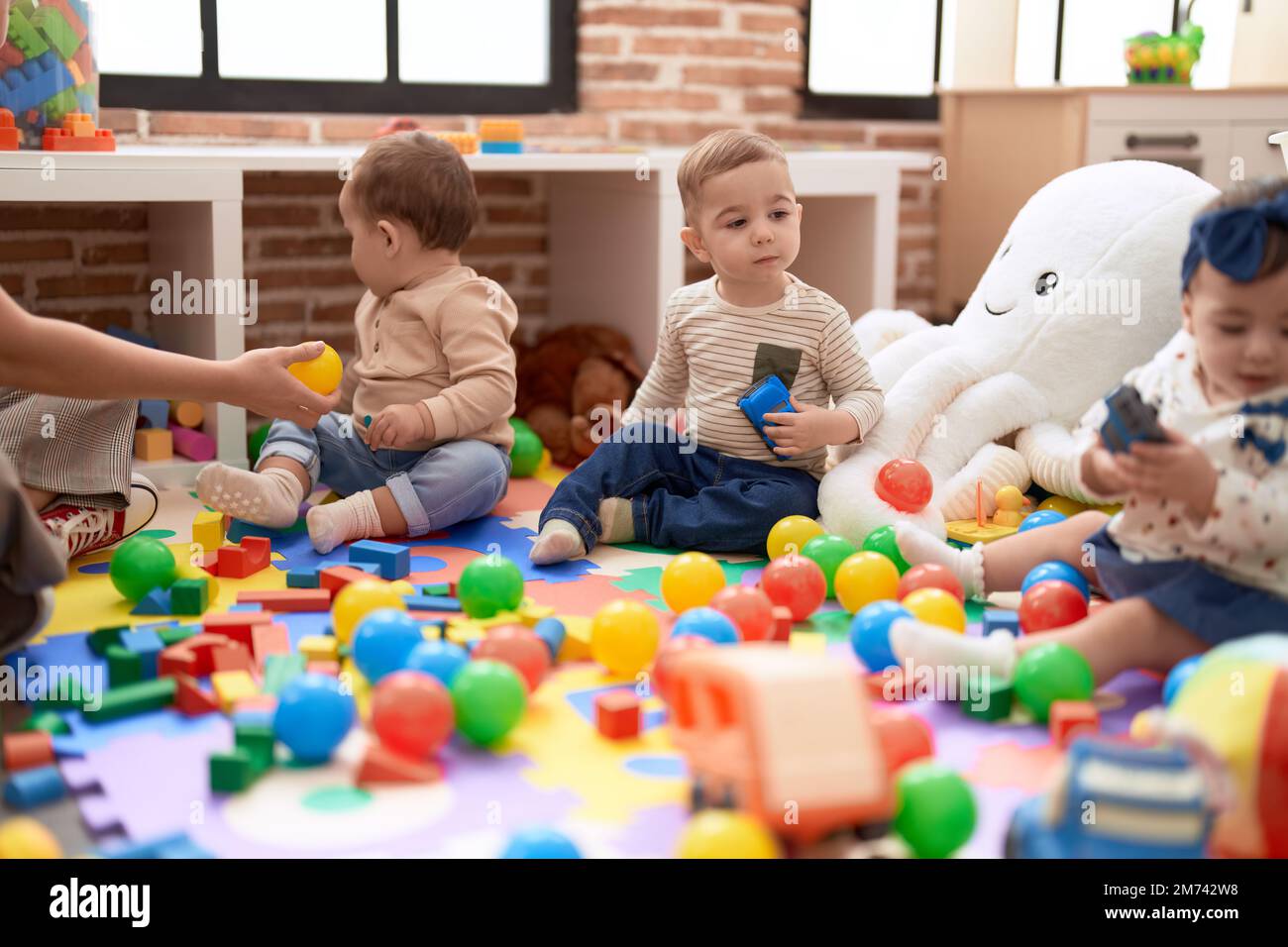 Group of toddlers playing with toys sitting on floor at kindergarten ...