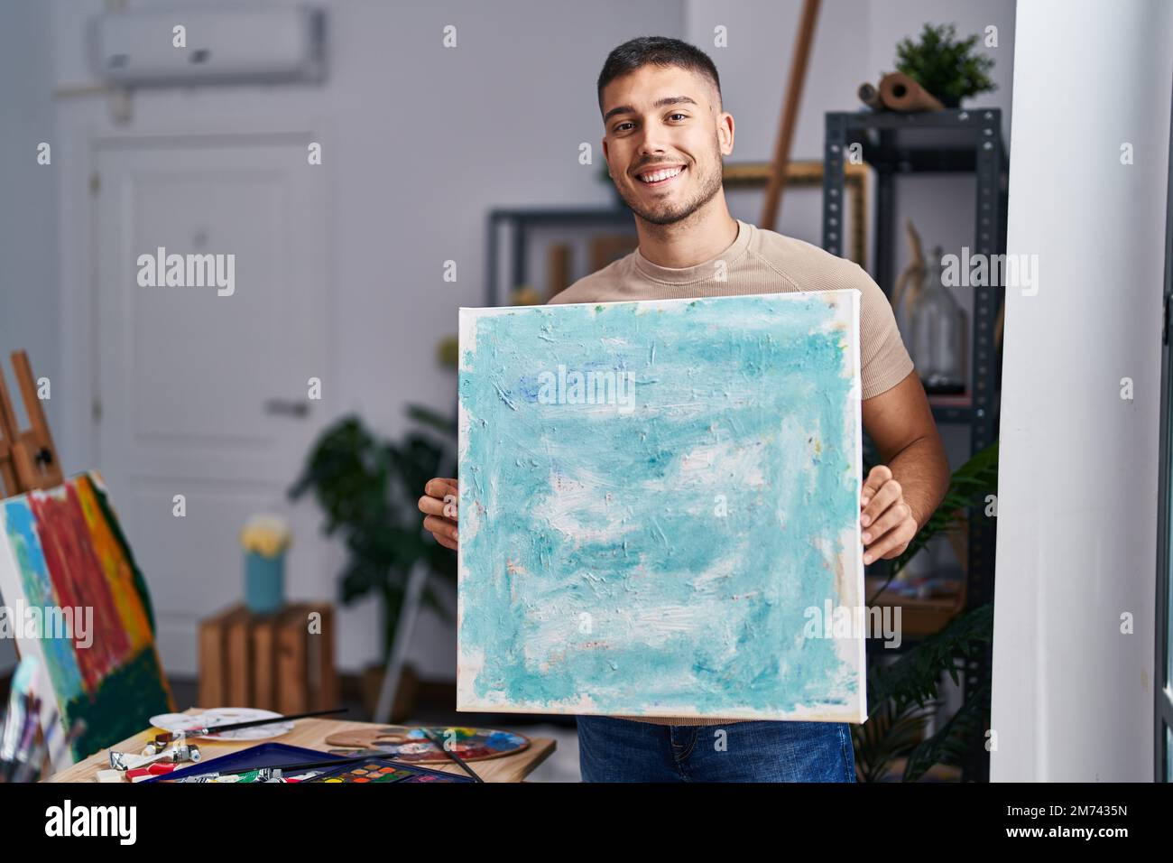 Young hispanic painter man holding canvas smiling with a happy and cool ...