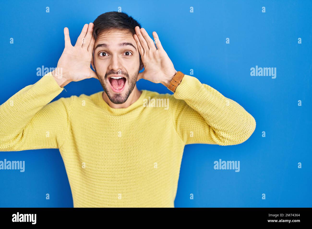 Hispanic man standing over blue background smiling cheerful playing ...