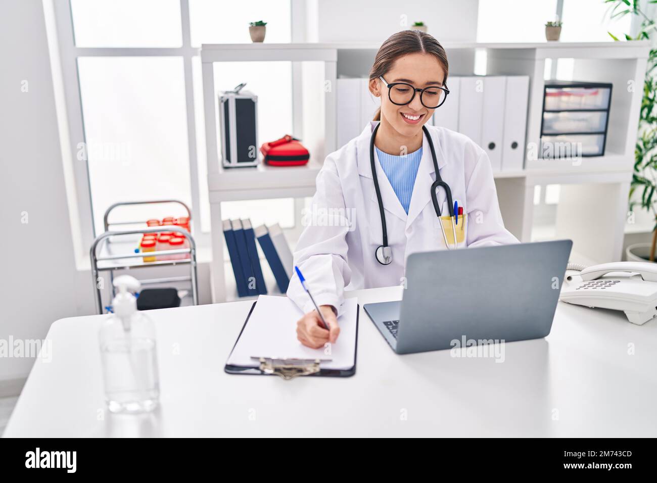 Young beautiful hispanic woman doctor using laptop writing medical ...