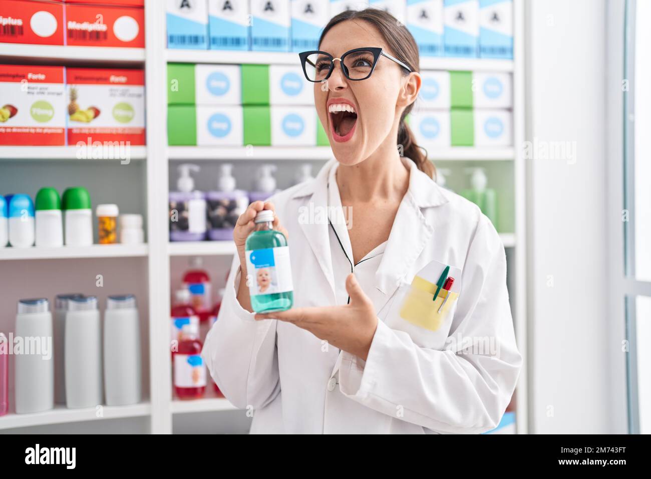 Brunette woman working at pharmacy drugstore holding cough syrup angry ...
