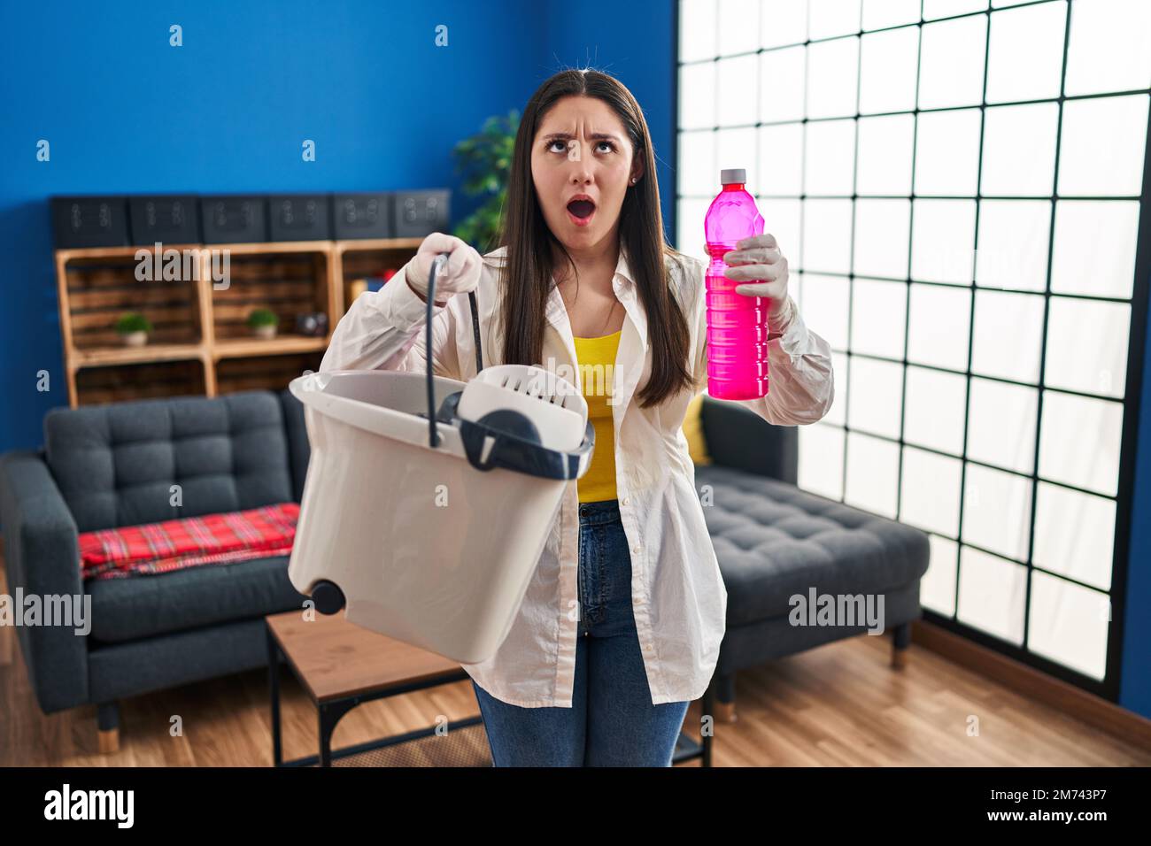 Young latin woman cleaning the house angry and mad screaming frustrated ...