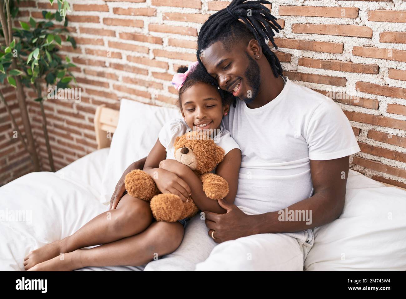 Father and daughter hugging each other sitting on bed holding teddy ...