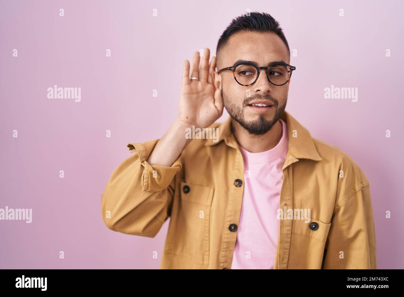 Young hispanic man standing over pink background smiling with hand over ...