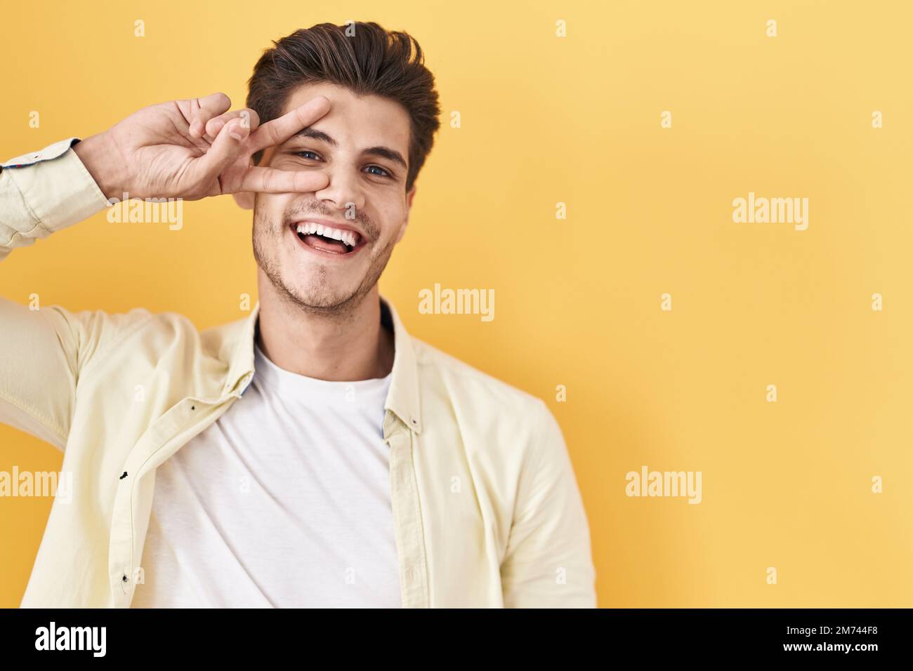 Young hispanic man standing over yellow background doing peace symbol ...