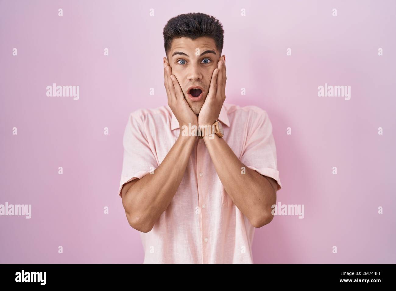 Young hispanic man standing over pink background afraid and shocked ...
