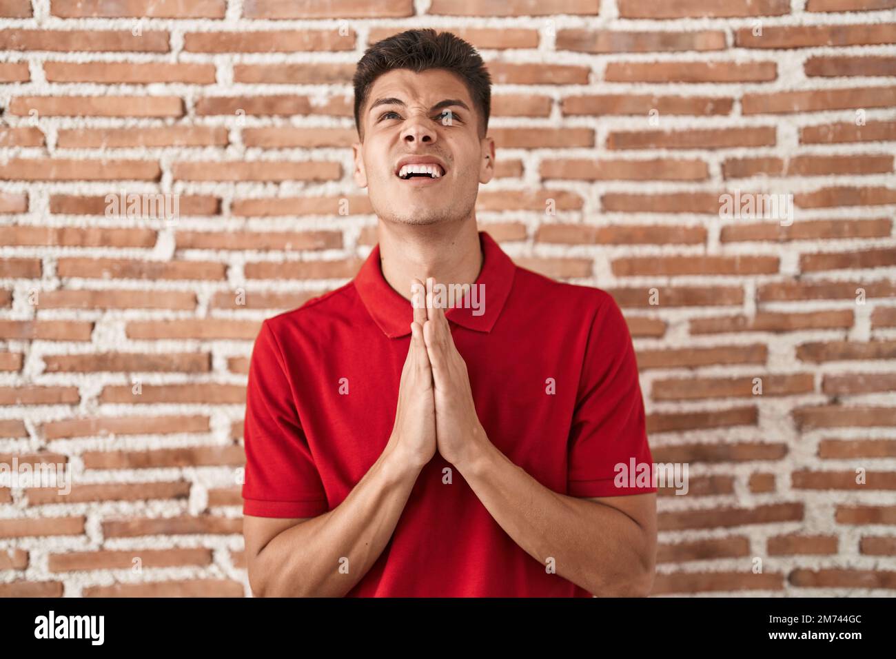 Young hispanic man standing over bricks wall begging and praying with ...