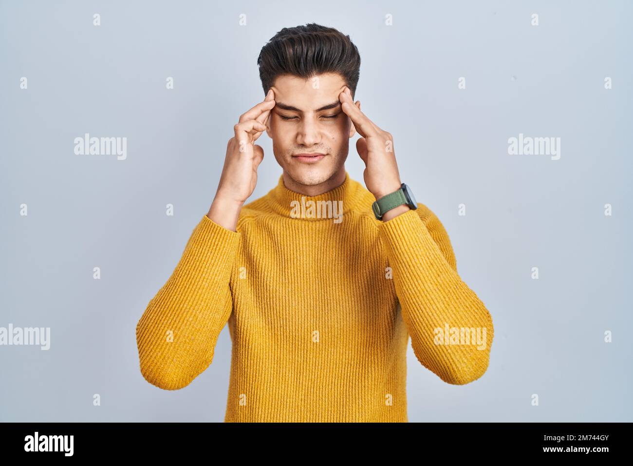 Young hispanic man standing over blue background with hand on head ...