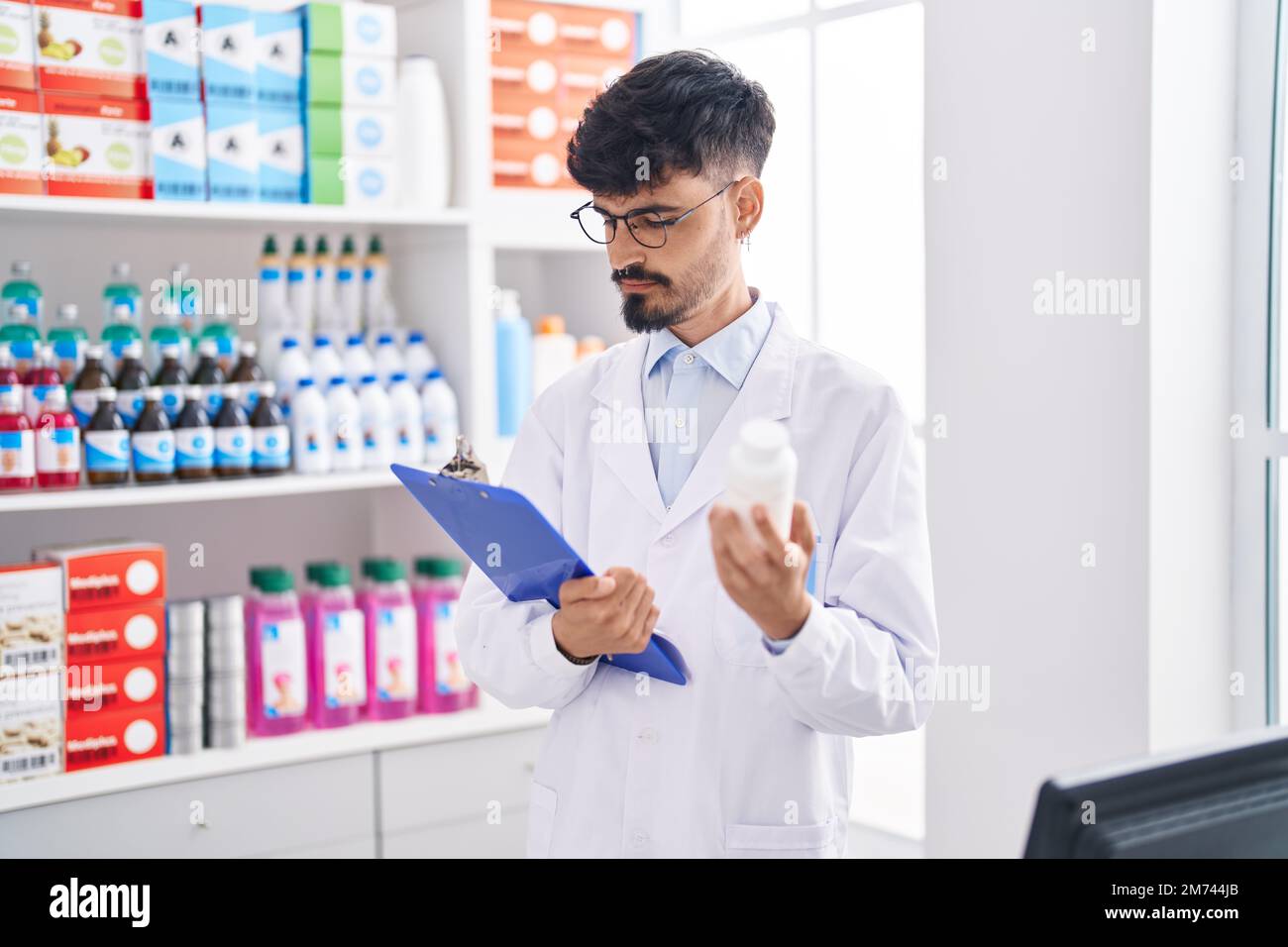 Young hispanic man pharmacist holding pills bottle and reading document ...