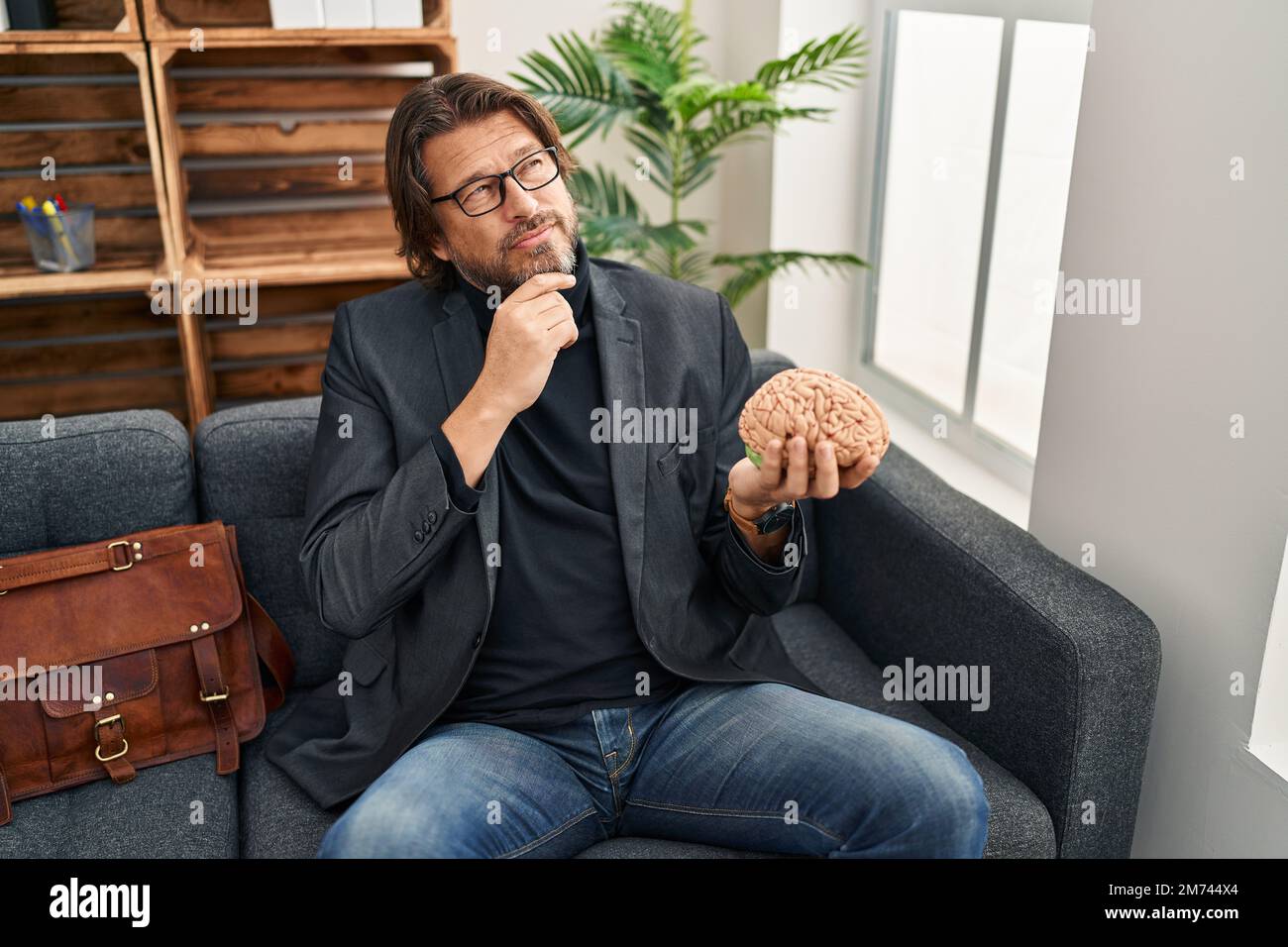 Handsome middle age man at consultation office holding brain serious ...