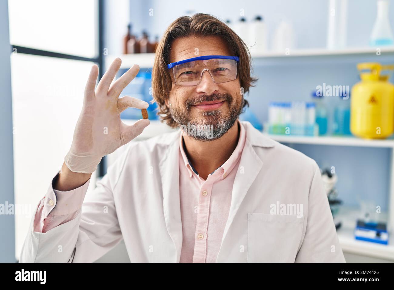 Middle age man scientist smiling confident holding pill at laboratory ...