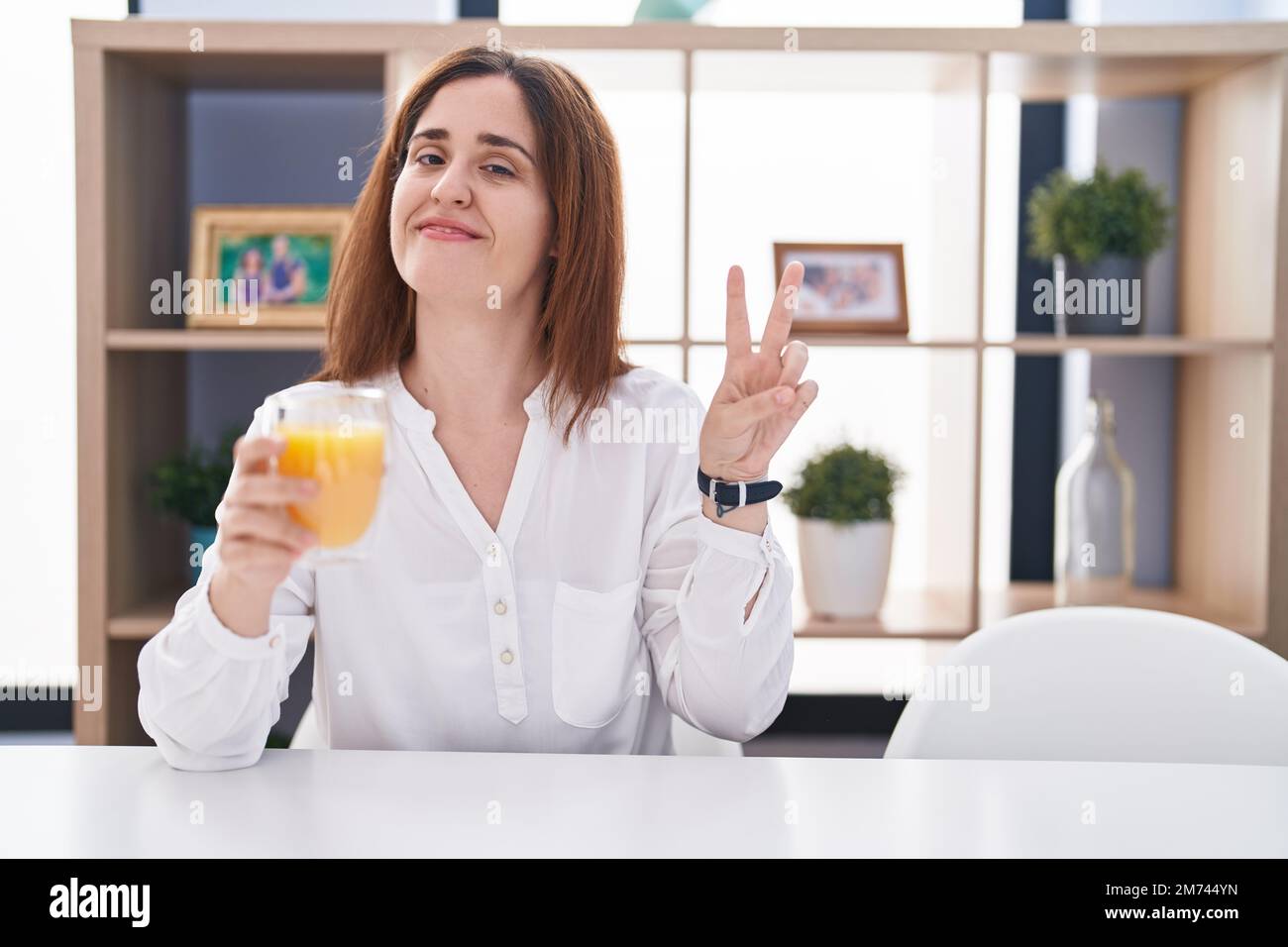 Brunette woman drinking glass of orange juice smiling looking to the ...