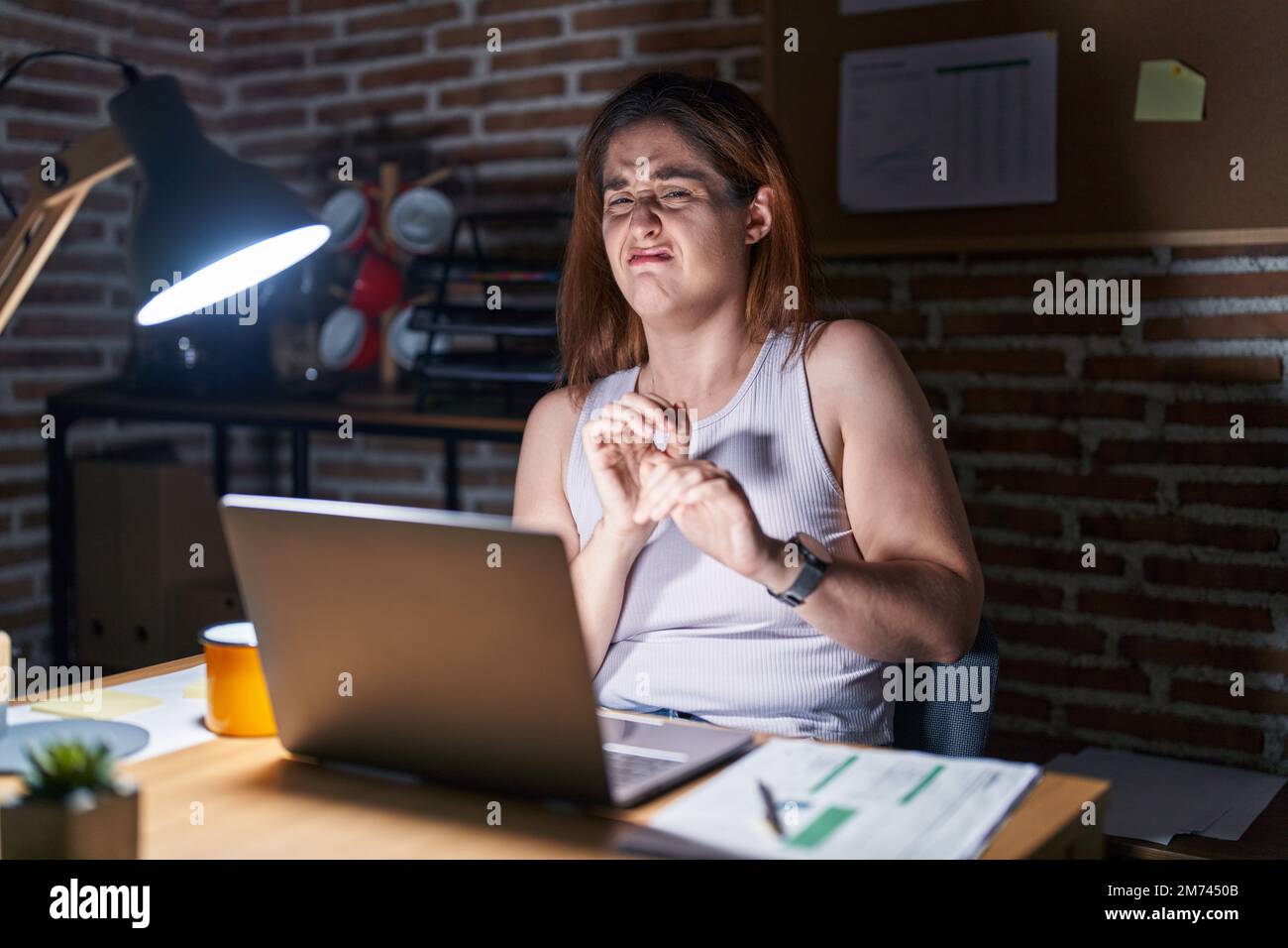 Brunette woman working at the office at night disgusted expression ...