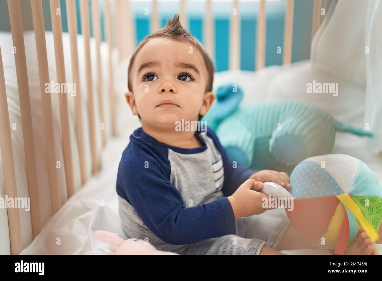 Adorable hispanic toddler sitting on cradle with relaxed expression at ...