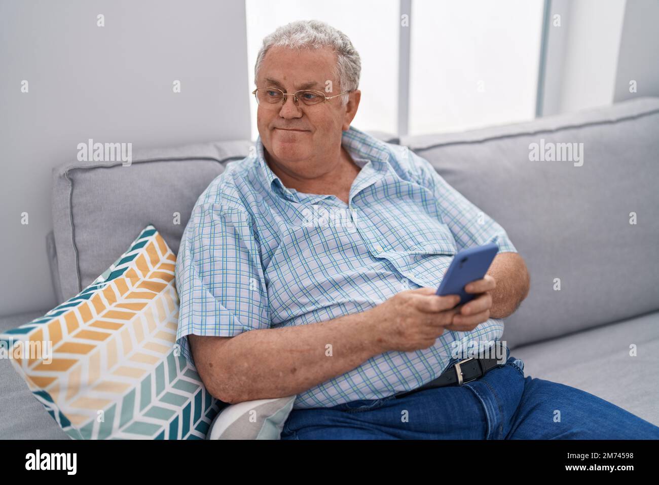 Middle age grey-haired man using smartphone sitting on sofa at home ...