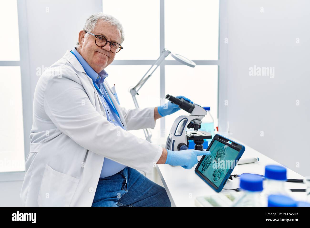 Middle age grey-haired man wearing scientist uniform looking embryology image touchpad at ...