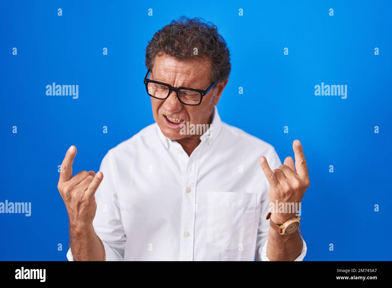 Middle age hispanic man standing over blue background shouting with ...