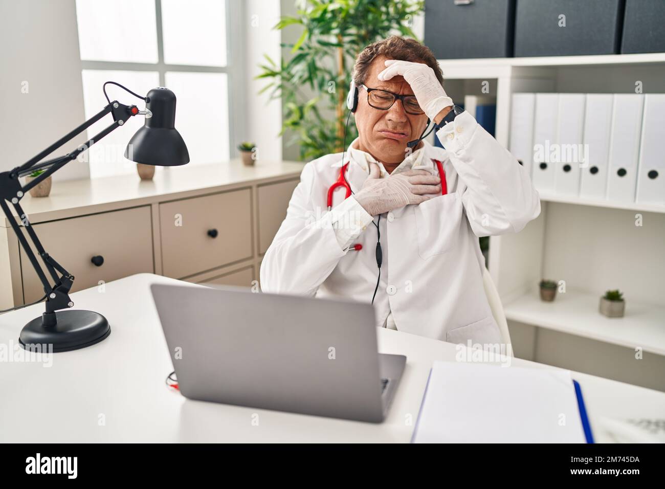 Senior doctor man working on online appointment touching forehead for ...