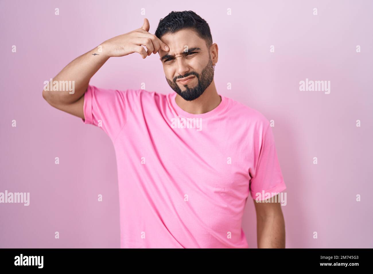 Hispanic young man standing over pink background pointing unhappy to ...