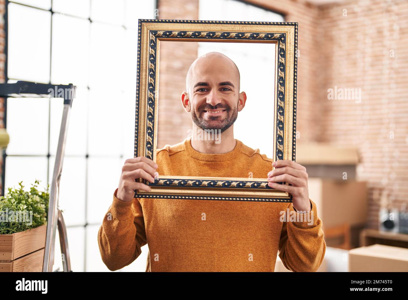 Young bald man with beard moving to a new home putting face inside ...