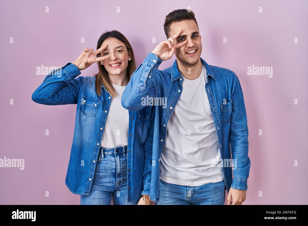 Young hispanic couple standing over pink background doing peace symbol ...