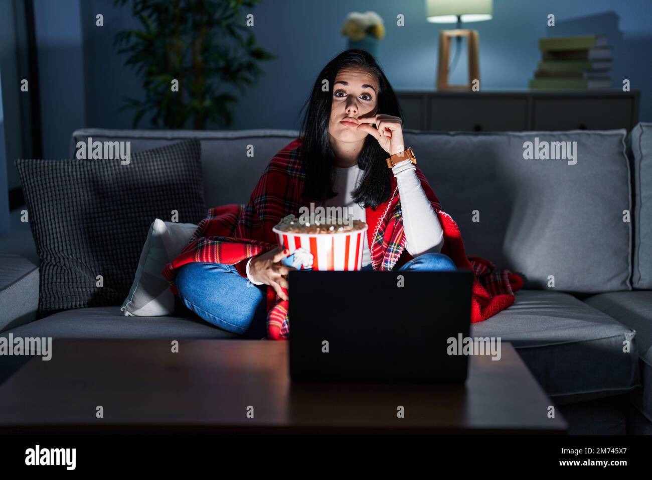 Hispanic woman eating popcorn watching a movie on the sofa mouth and ...