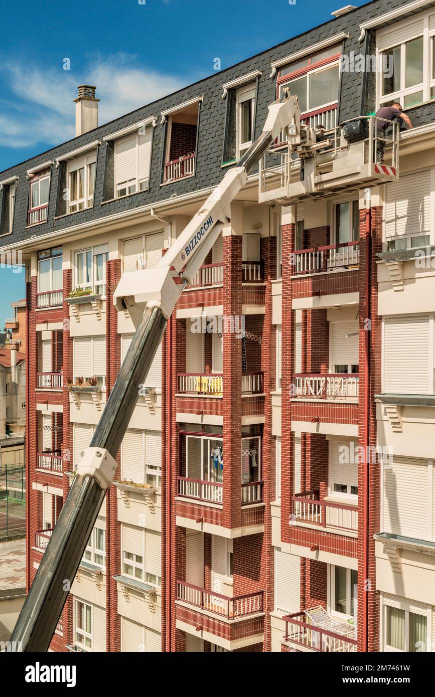 Worker on crane with lifting basket repairs the wall of the building ...