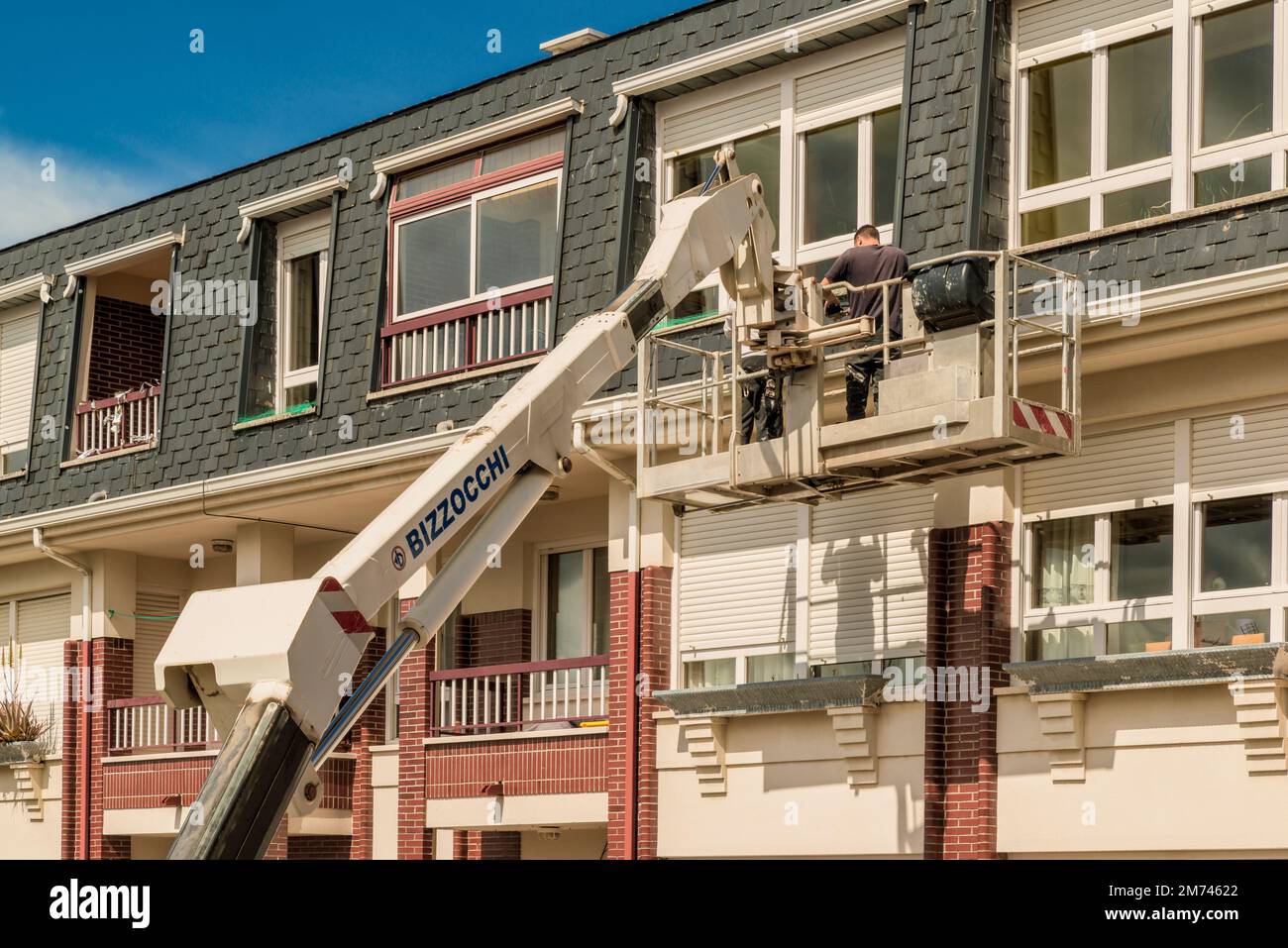 Worker on crane with lifting basket repairs the wall of the building ...