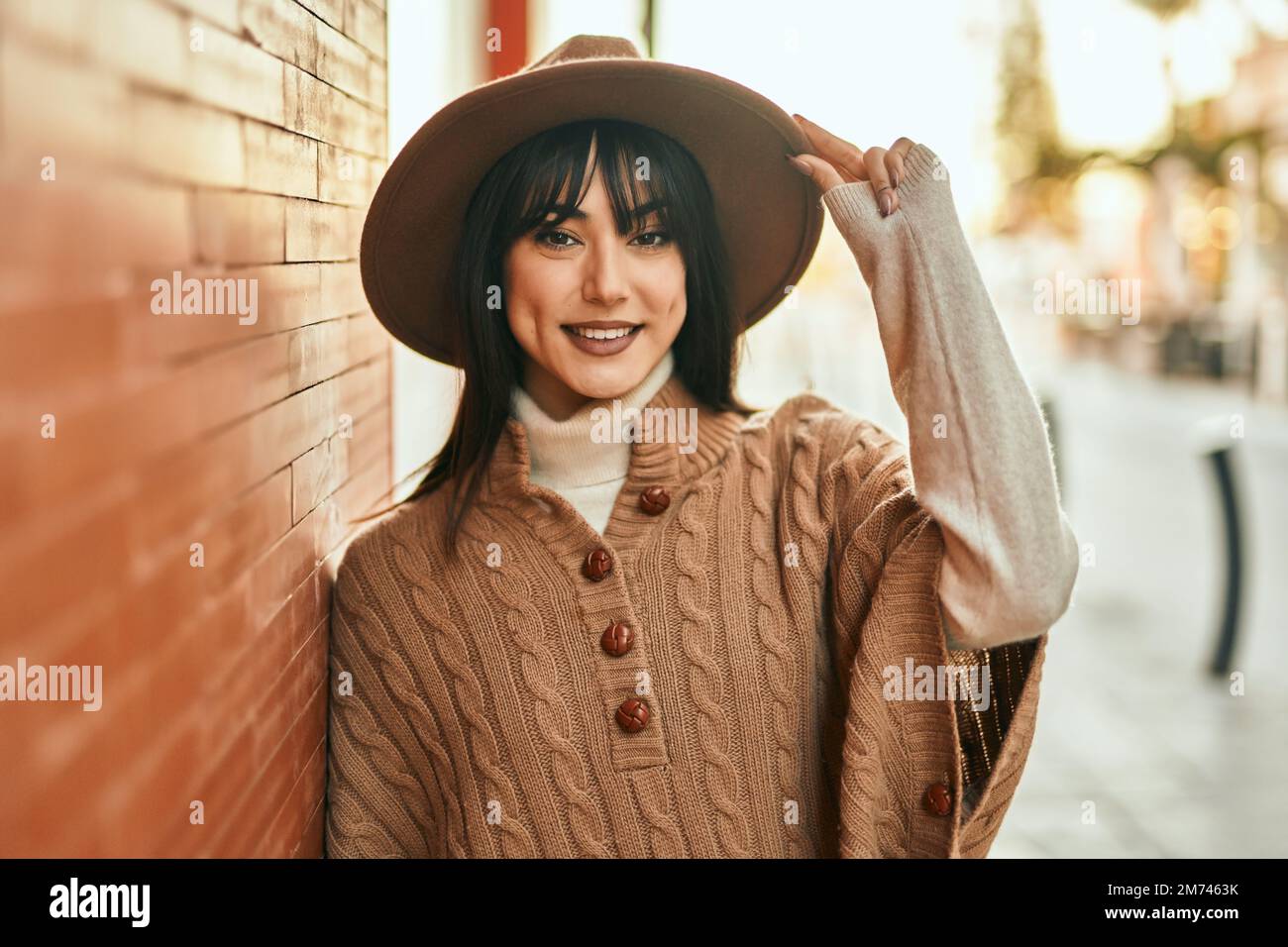 Brunette woman wearing winter hat smiling leaning on bricks wall Stock ...